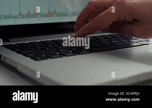 A image of a hand typing on a laptop keyboard while a graph with data ...