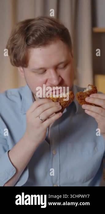 Young man savoring fried chicken while sitting comfortably on living ...