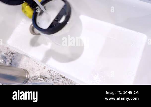 Yellow-gloved hands are seen washing dishes, scrubbing diligently in a ...