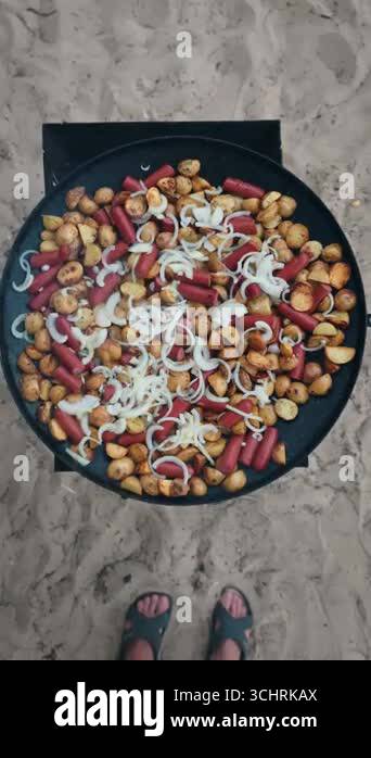 A top-down vertical shot of a large round pan on a grill, cooking ...