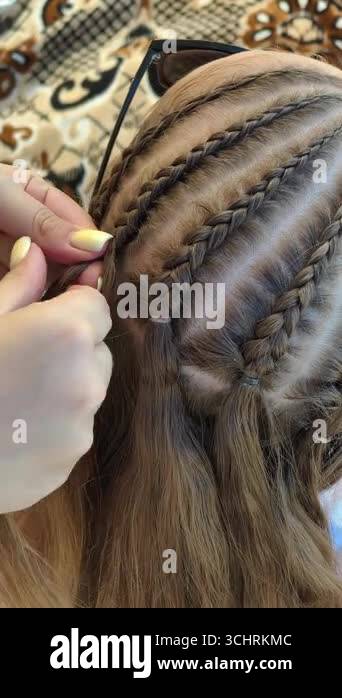 Close-up view of a professional hairstylists hands meticulously weaving thin cornrow braids on a ...