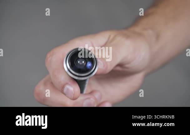 Macro view of a hand holding a compact peephole camera. The focus is on ...