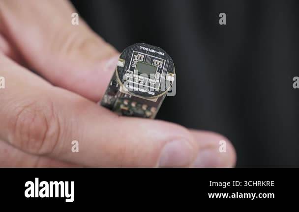 Close-up shot shows a hand holding a tiny digital camera module. The ...