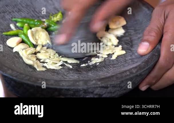 Grinding garlic and green pepper with mortar and pestle, close up ...
