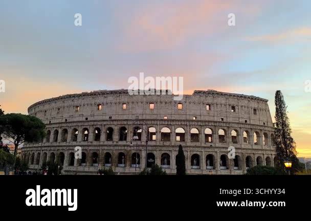 As the sun sets behind the Colosseum in Rome, hues of orange and pink ...