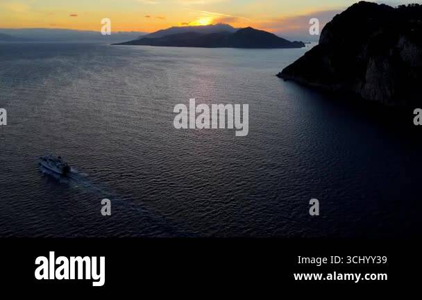 As the sun descends beyond the mountains, a small boat glides through ...