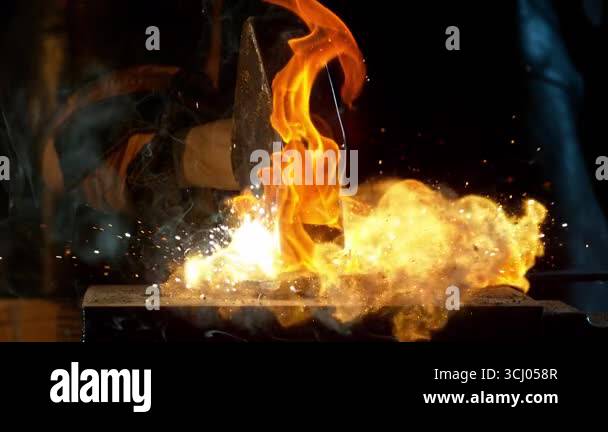 Close-up of blacksmith forging glowing hot iron on anvil with flying sparks. Super slow motion ...