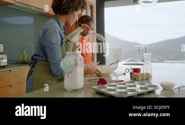 Mother and daughter scooping flour, cracking egg, stirring batter into ...