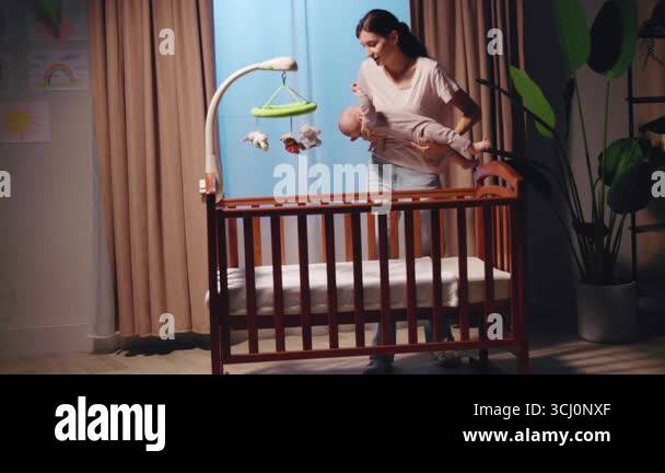 At night smiling young mother with her little baby lying in cradle ...