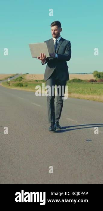 A businessman in a formal suit walks a peaceful rural road, skillfully ...