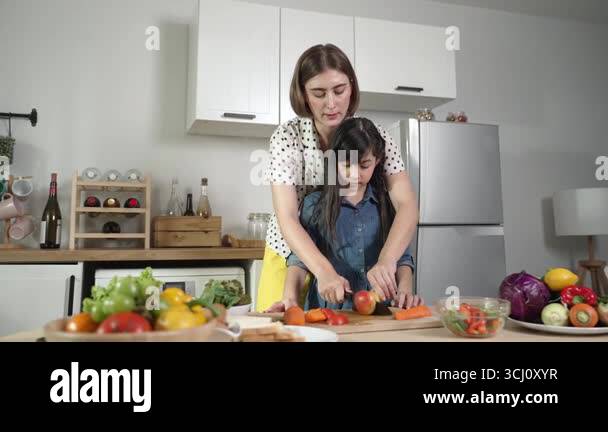 Smart caucasian mother and asian girl cooking together and chopping ...