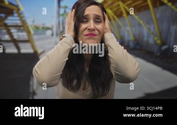 Woman appears stressed, covering her ears on an urban street ...