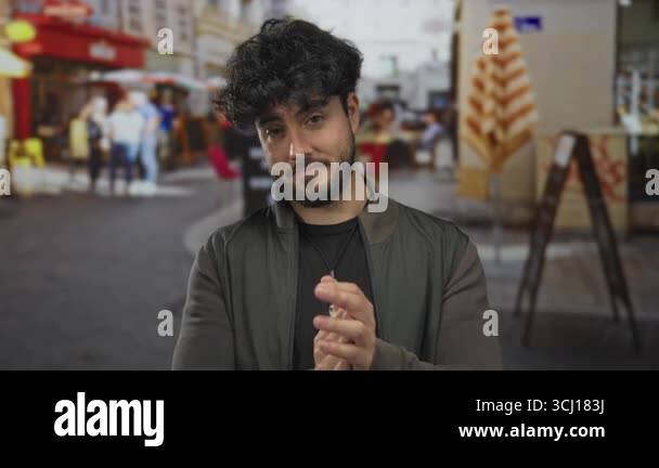Young man with beard clapping on a bustling street with blurred people ...