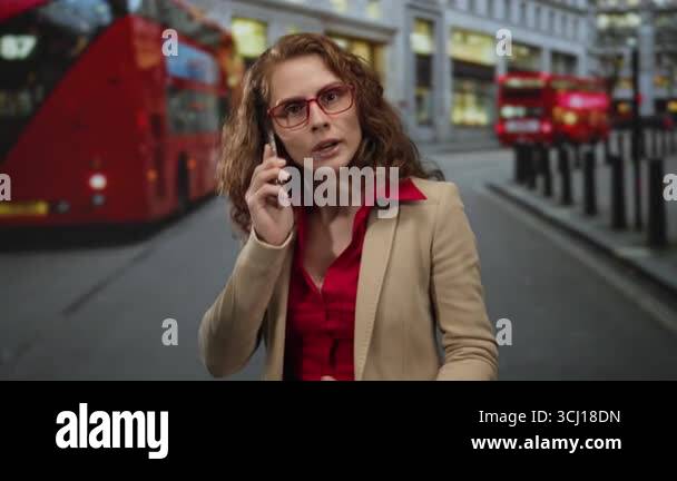 Woman talking on smartphone in urban street with double-decker buses ...