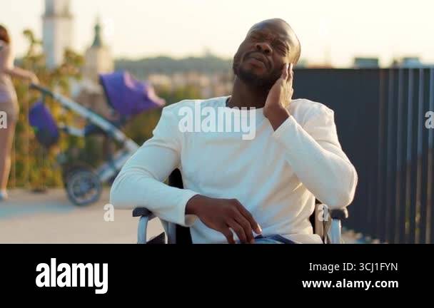 Close up young man use headphones speaking phone on a wheelchair in a ...