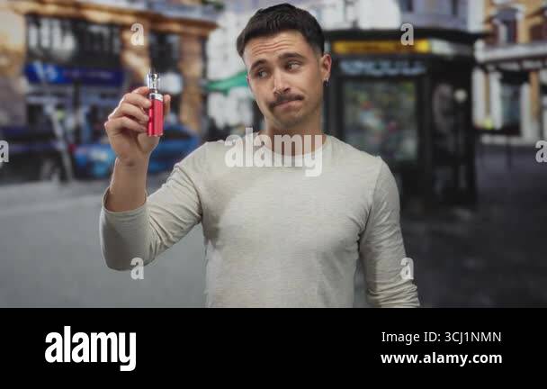 Young hispanic man holding vape with thumbs down on city street ...