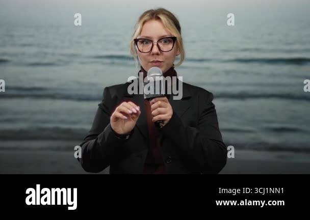 Young woman reporter with microphone speaking on beach seaside with sea ...