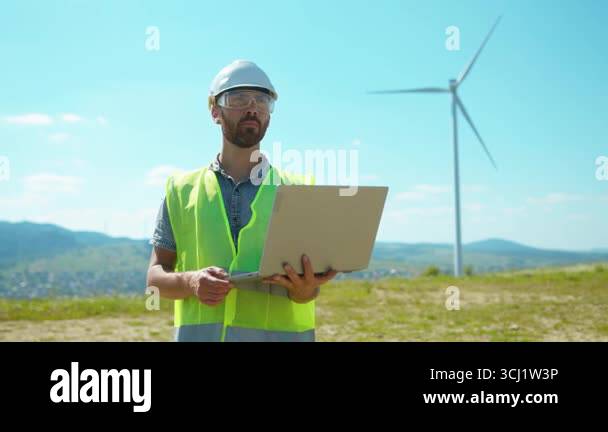 In uniform man engineers use laptop stand near windmills in fields ...