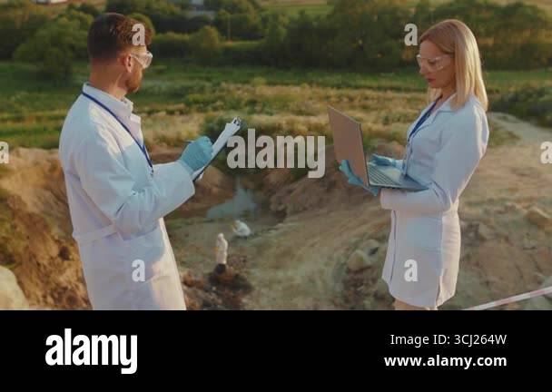 Close up ecology experts use laptop in protection wear working on land relief talking chemicals ...