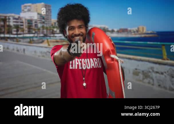 Lifeguard man smiling and pointing at promenade with sea background ...