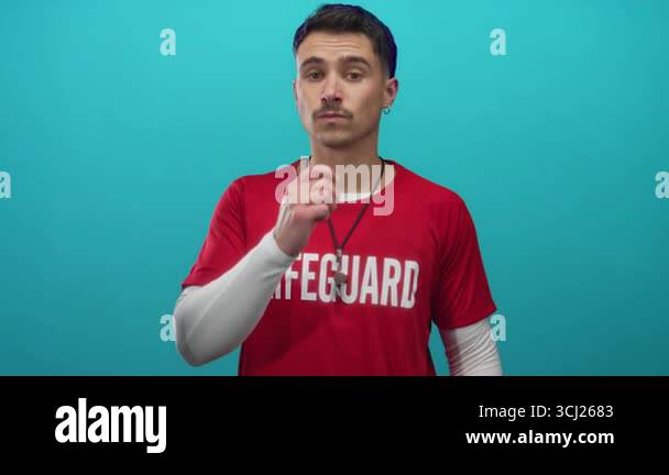 Young hispanic lifeguard man playfully sends a kiss while wearing a red ...