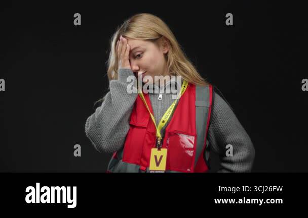 Blonde woman smiling in red volunteer vest against black background ...