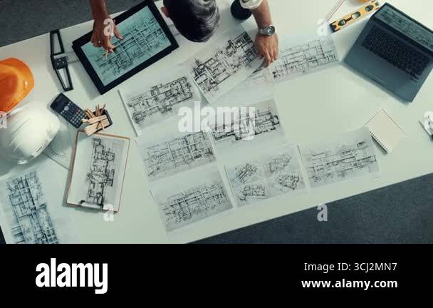 Top down view of engineer looking at tablet while using laptop to ...