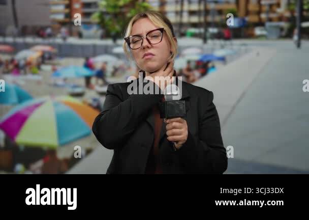 Woman reporter at seaside holding microphone while adjusting glasses ...