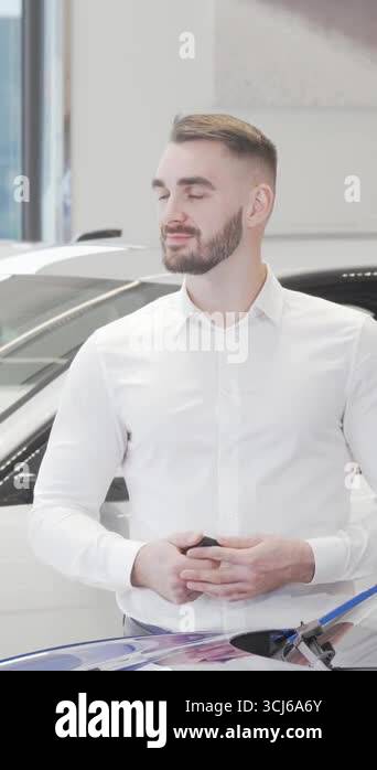 A dapper young man stands confidently in a modern car dealership ...