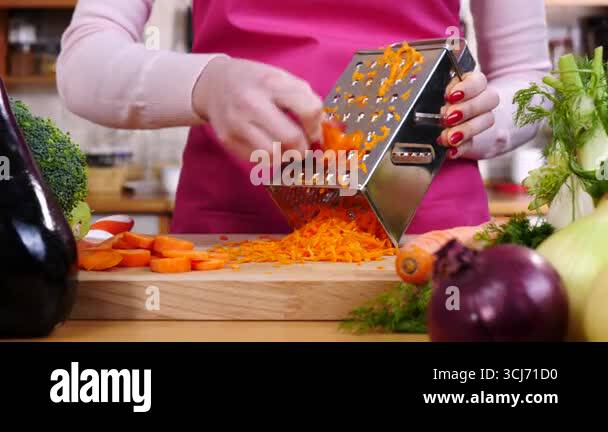 Close up of woman hand grating carrot on kitchen board in slow motion ...
