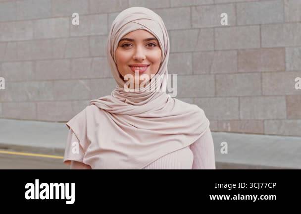 A young Muslim woman wearing a stylish beige hijab smiles confidently ...