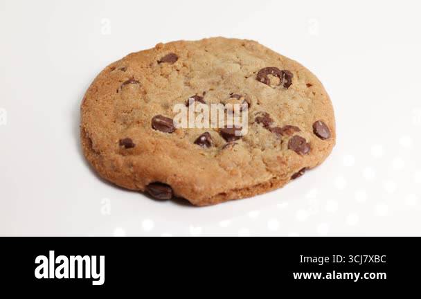 A hand reaches for and picks up a chocolate chip cookie from a white ...