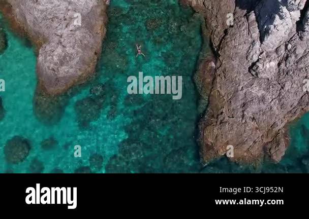 Girl swimming in the sea among rocky cliffs, aerial view. Crystal clear ...