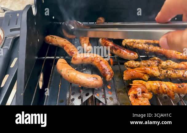 Person grilling meat skewers, sausages, and corn on a gas barbecue ...