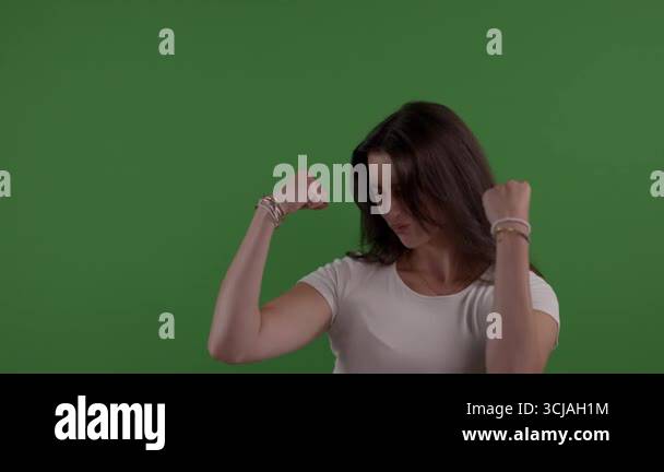 Studio shot of a young woman flexing her biceps on a green screen ...