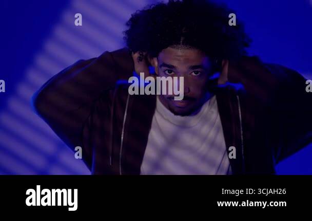 Portrait of a young artist posing under blue light holding his head ...