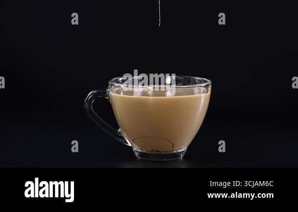 Honey drips into a glass cup of coffee against a black background ...