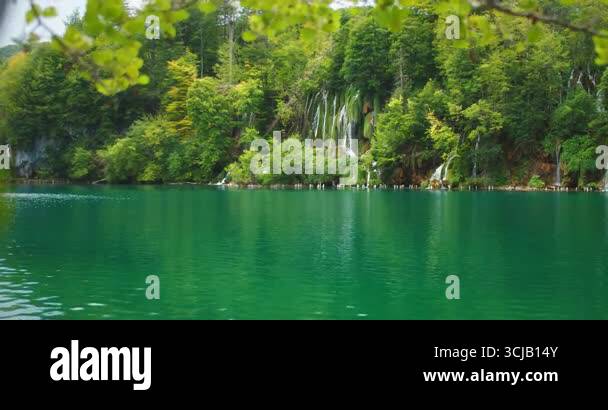 Waterfalls cascade down lush cliffs into a vibrant lake in Plitvice ...