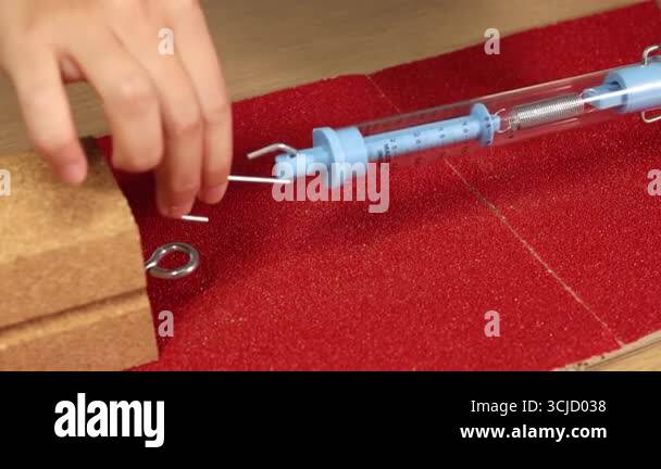 A hand conducts a friction test with a spring scale on a red textured ...