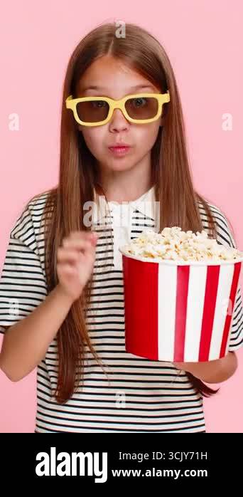 Young child girl happily eats popcorn, watching an entertaining cartoon ...