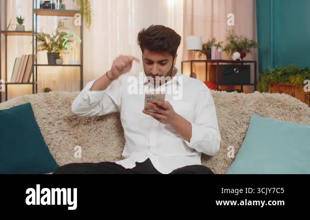 Indian man at home on sofa talking on speakerphone, gesturing intensely ...