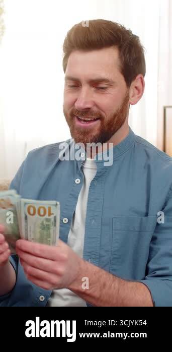 Young man at home holding a stack of dollar cash banknotes, counting ...