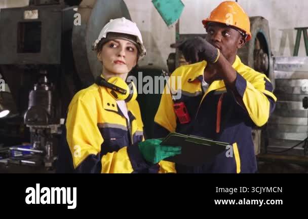 Two male and female factory mechanics operate metal stamping machines ...