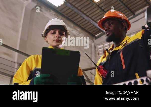 Two male and female factory mechanics operate metal stamping machines ...