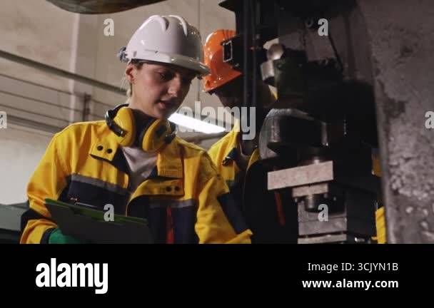 Two male and female factory mechanics operate metal stamping machines ...