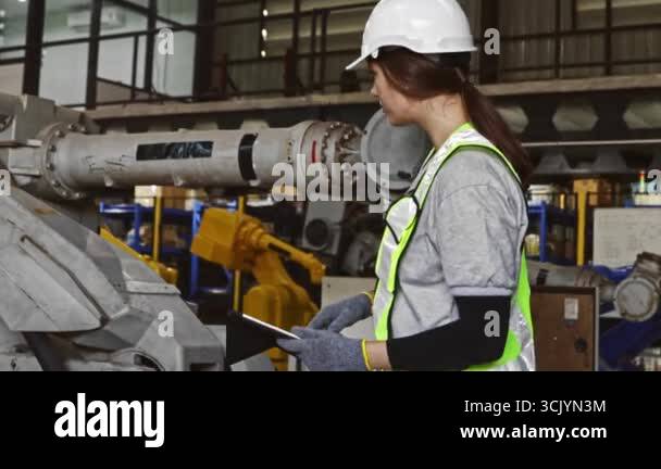 Female robot engineer holding laptop walks inspect robot hydraulic TIG ...