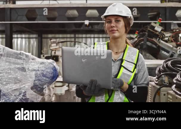 Female robot engineer holding laptop walks inspect robot hydraulic TIG ...