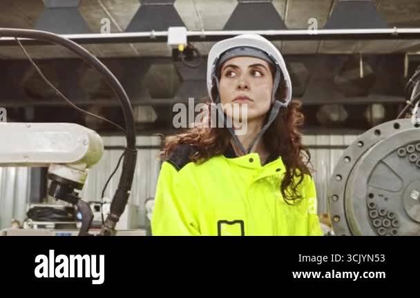 Hispanic female robotics engineer wearing safety helmet intently ...