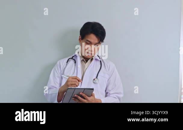 Portrait of handomse asian male doctor holding a medical examination tablet recording patient ...