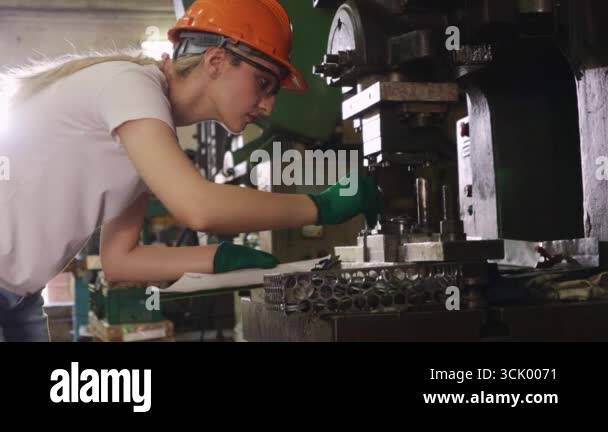 Female lathe operator wearing hard hat and safety glasses uses a wrench ...